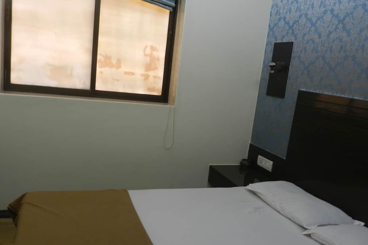 Quarto com cama, mesa de cabeceira, telefone fixado na parede e janela com cortina.