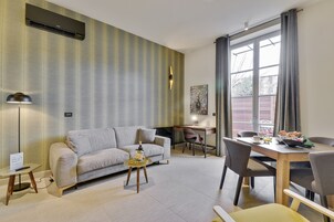 Uma sala de estar moderna com um sofá, uma mesa de jantar com cadeiras, um abajur e uma janela grande com cortinas.
