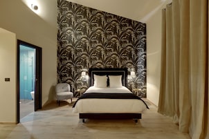 Quarto moderno com uma cama grande, uma cadeira, uma mesa de cabeceira e um banheiro visível por uma porta aberta.