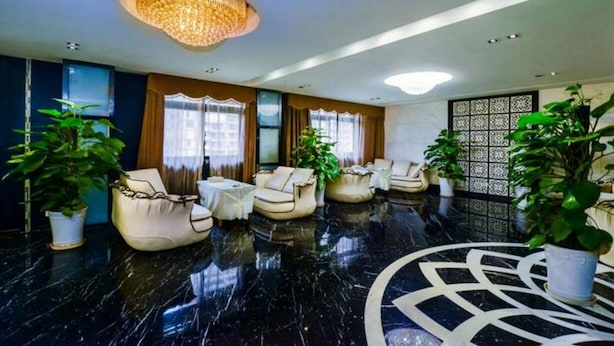 Um hall espaçoso com piso de mármore preto, um grande lustre e vários espaços de estar com plantas em vasos.