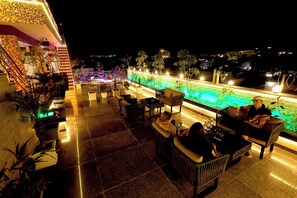 Uma área de estar externa com mobiliário de vime e uma piscina com bordas iluminadas.