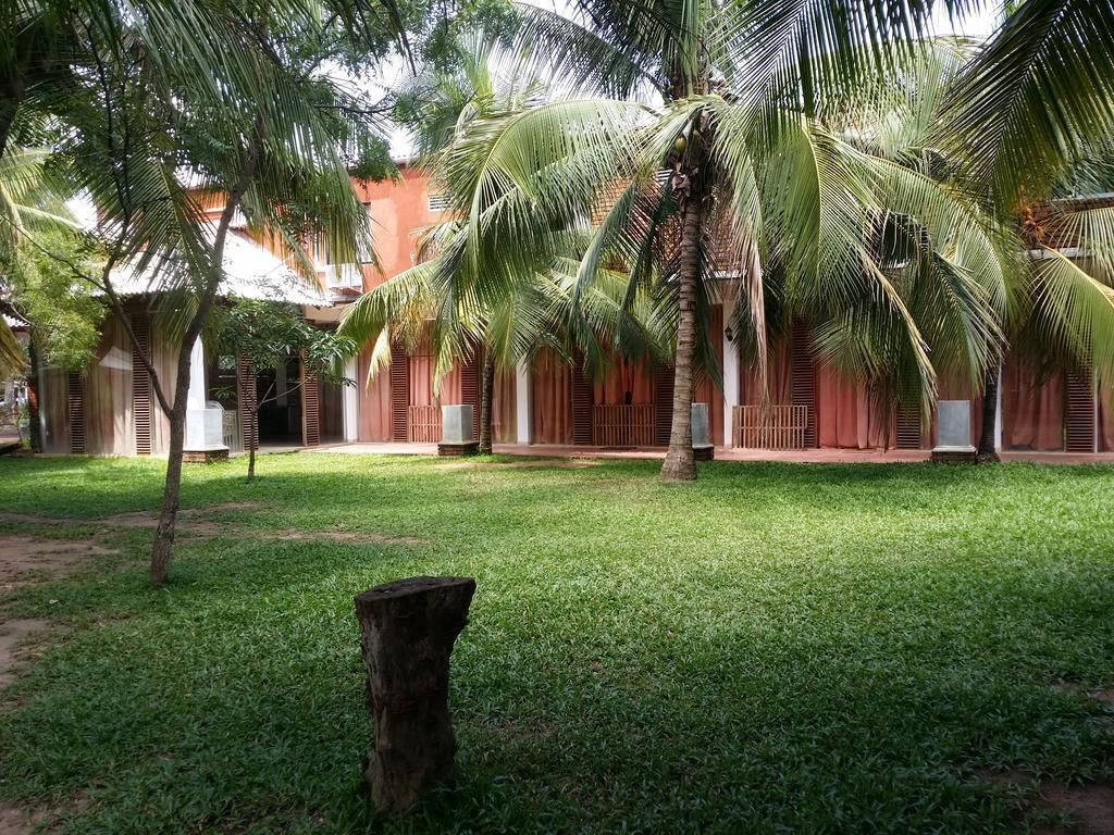 Um pátio com palmeiras e um edifício com paredes vermelhas e janelas com contraventanas brancas.
