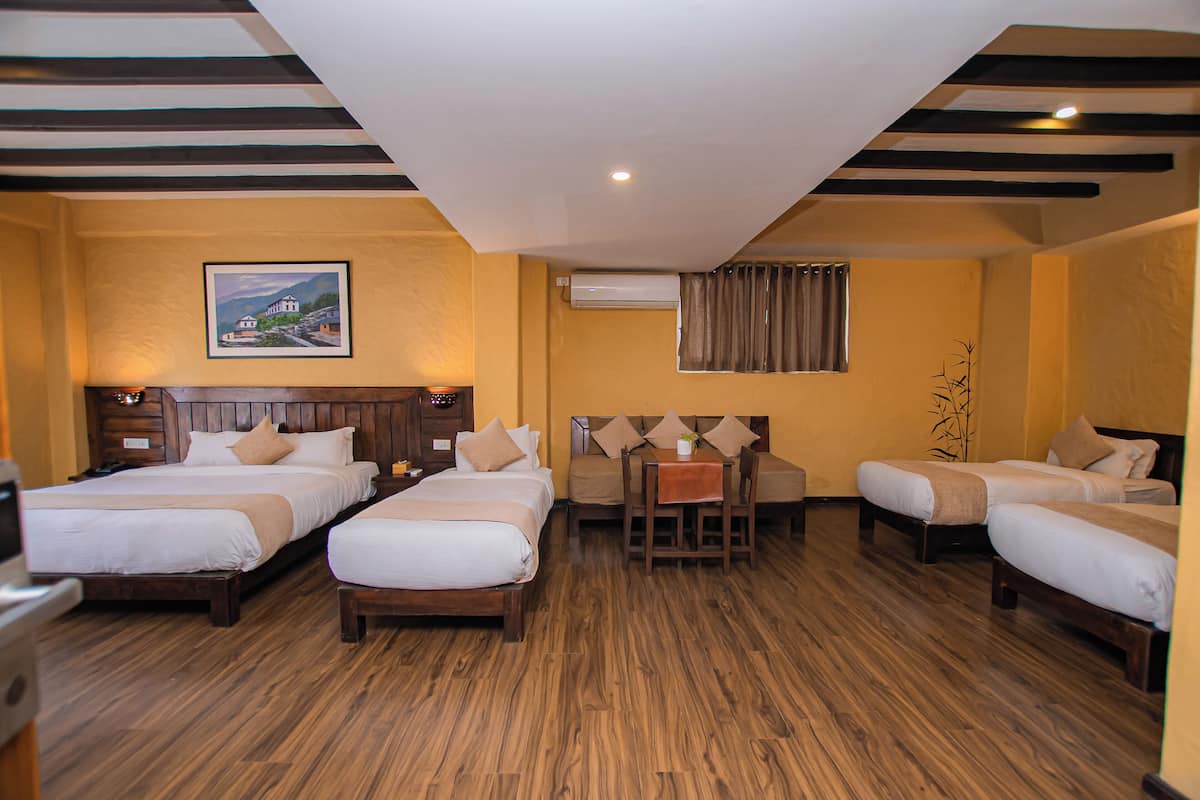Quarto de hotel com quatro camas, piso de madeira, uma mesa de jantar e um quadro na parede.