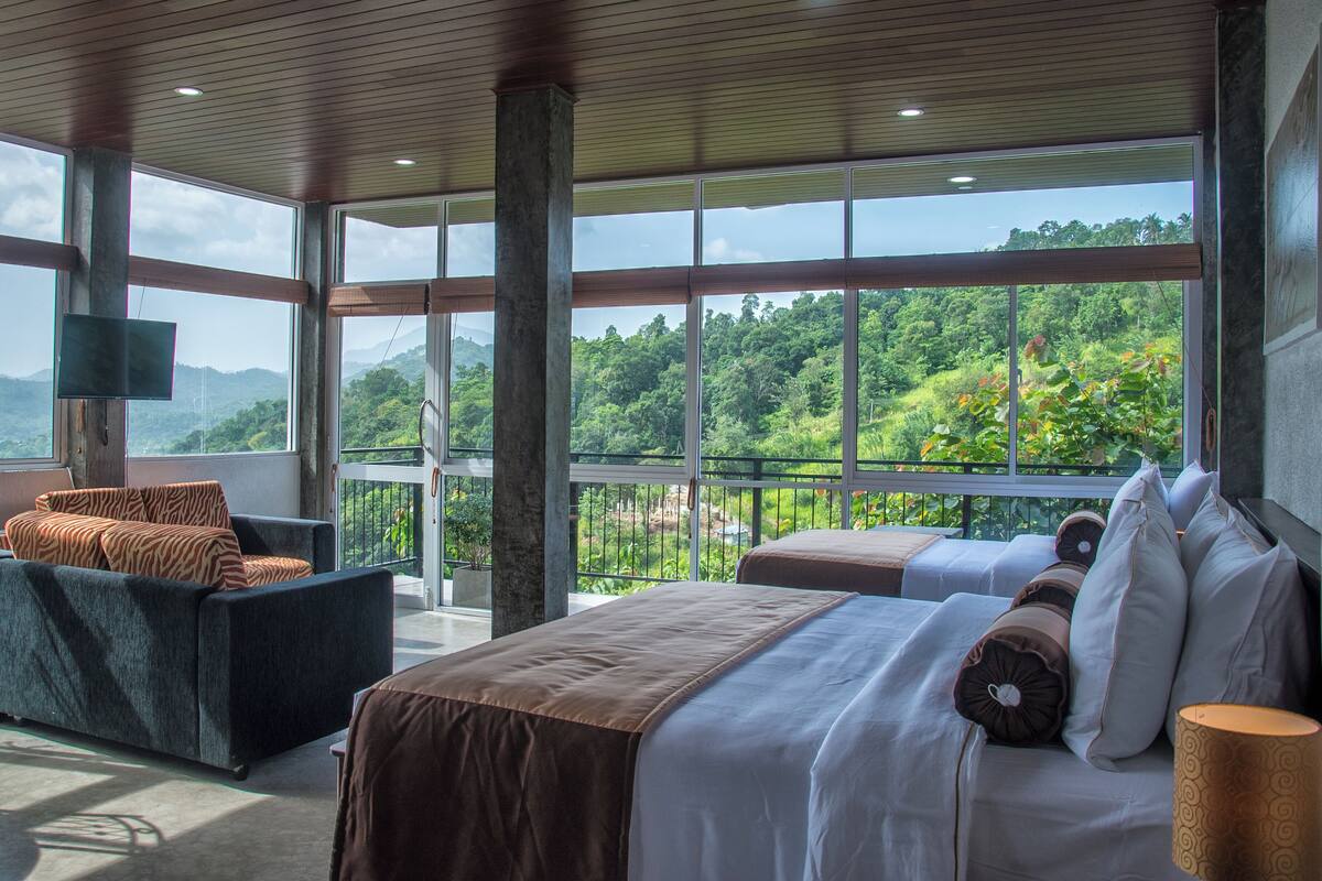 Um quarto espaçoso com uma cama grande, um sofá e uma varanda com vista para vegetação exuberante e montanhas.