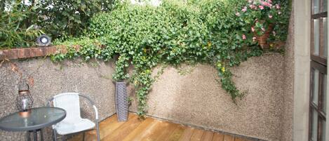 Um deck de madeira com uma mesa e cadeiras, cercado por um muro coberto de plantas trepadeiras e flores.