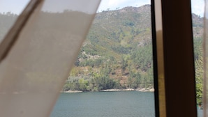 Vista pela janela com montanha e ponte ao fundo.