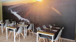 Restaurante com mesas preparadas para refeições, um mural com um pôr do sol sobre montanhas e design de interiores moderno.