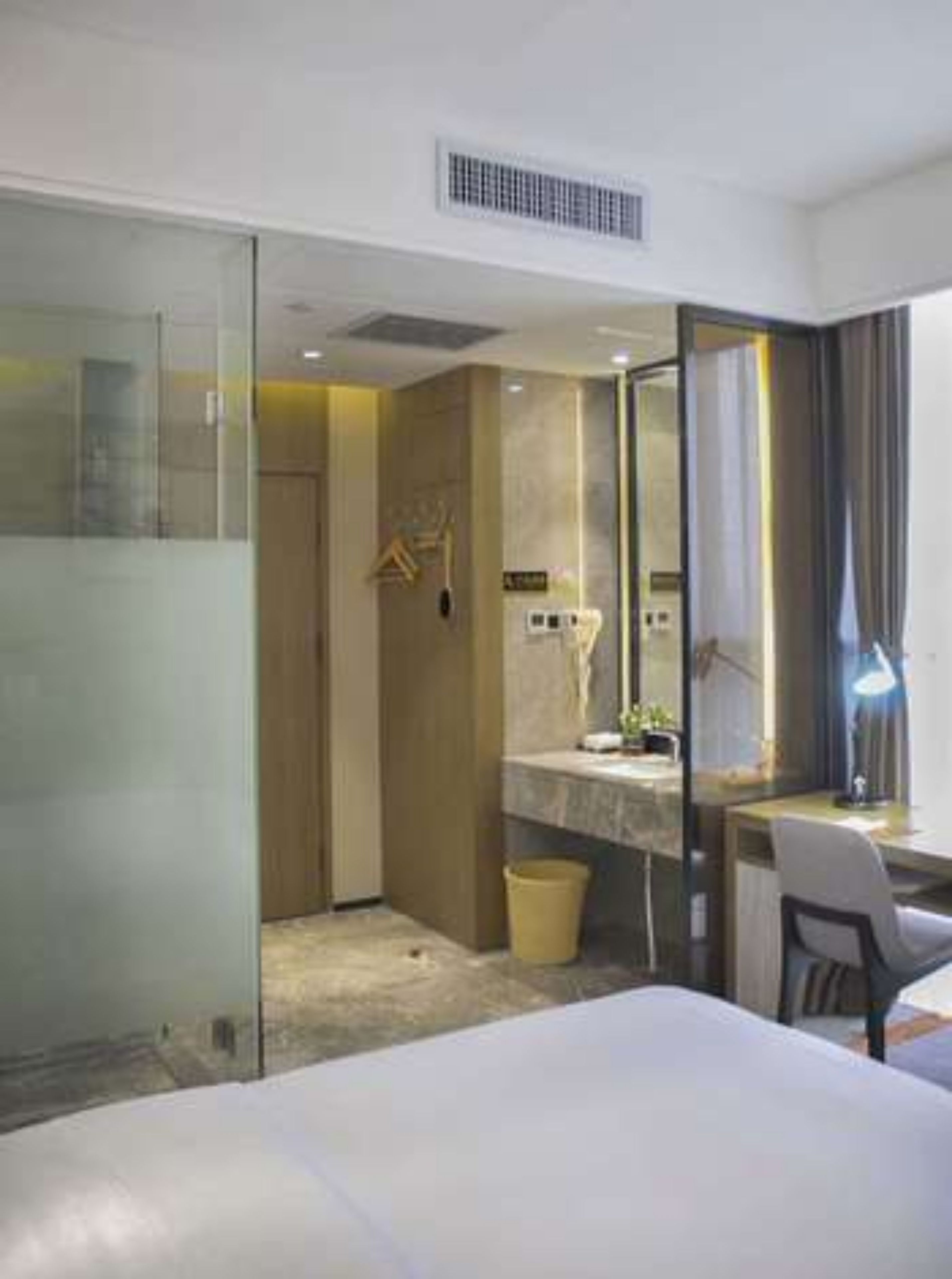 Quarto de hotel com uma cama, uma escrivaninha, uma cadeira, um espelho, uma pia e um cesto de lixo.