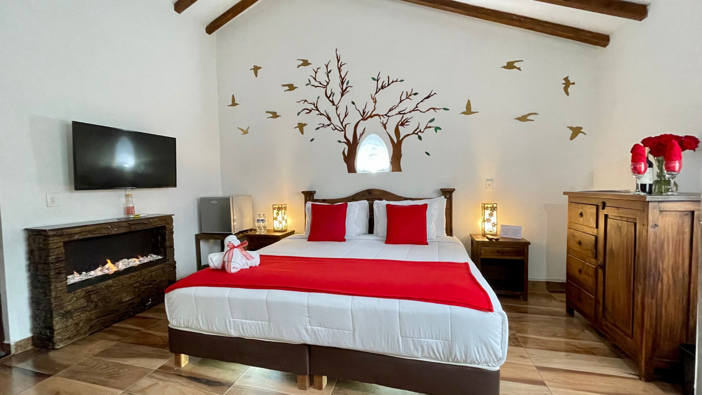 Quarto com cama, televisão, lareira e decoração de parede com uma árvore e pássaros.