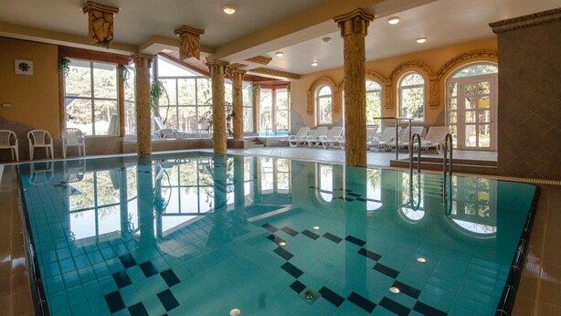 Piscina interior com água azul cristalina, cercada por colunas e grandes janelas.