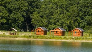 Uma fileira de cabanas de madeira à beira de um lago, com nenúfares e vegetação ao primeiro plano.