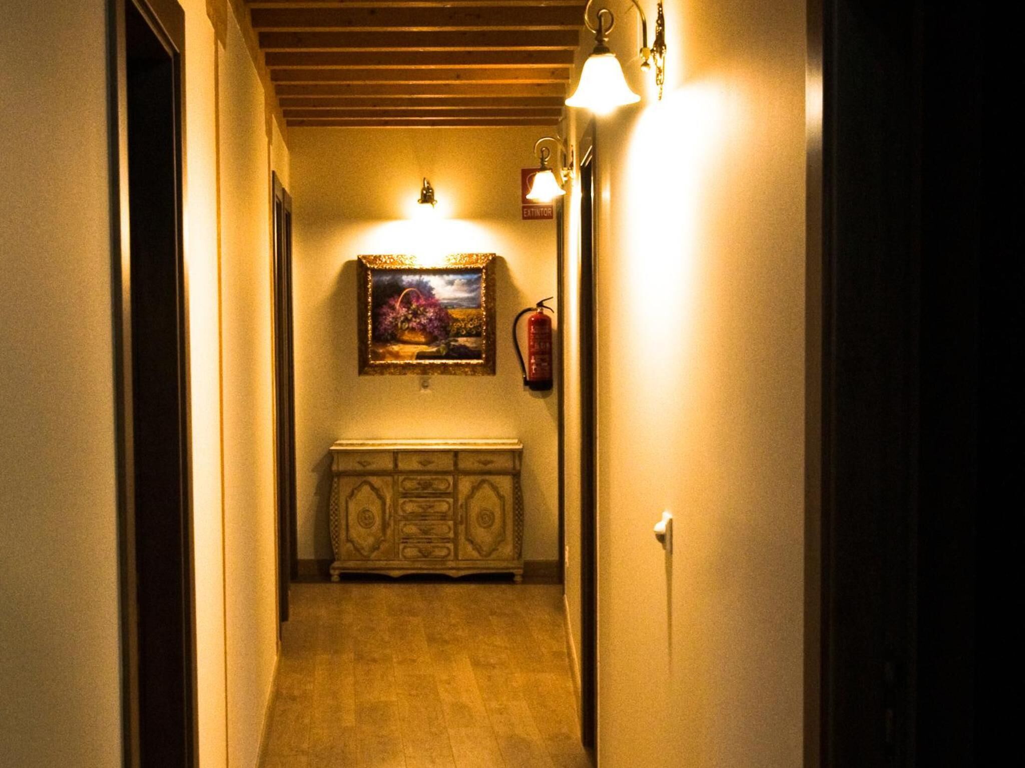 Um corredor com teto de madeira, luminária fixada na parede, quadro emoldurado e extintor de incêndio.