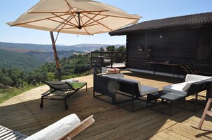 Um deck de madeira com móveis de exterior, um grande guarda-sol e vista para o campo.