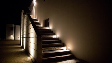 Uma escadaria com corrimãos e degraus iluminados, levando a uma porta no topo.