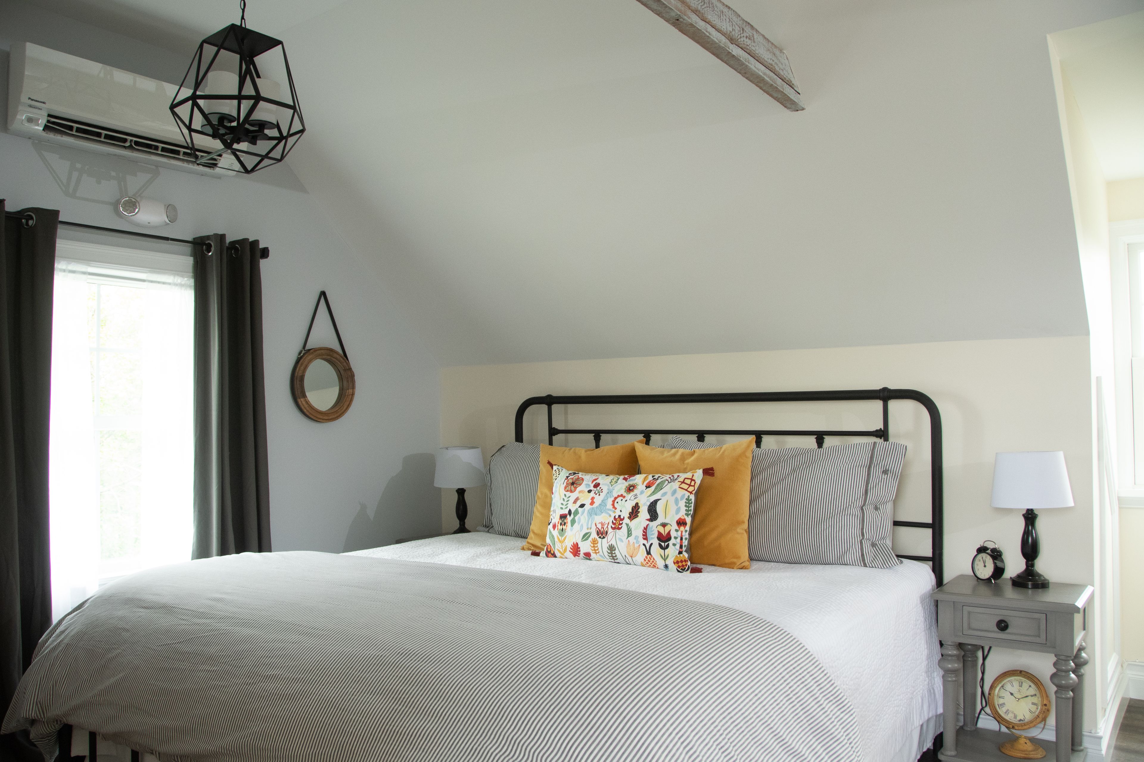Uma cama bem arrumada com roupa de cama listrada, um travesseiro decorativo, uma mesa de cabeceira com abajur e um relógio fixado na parede.