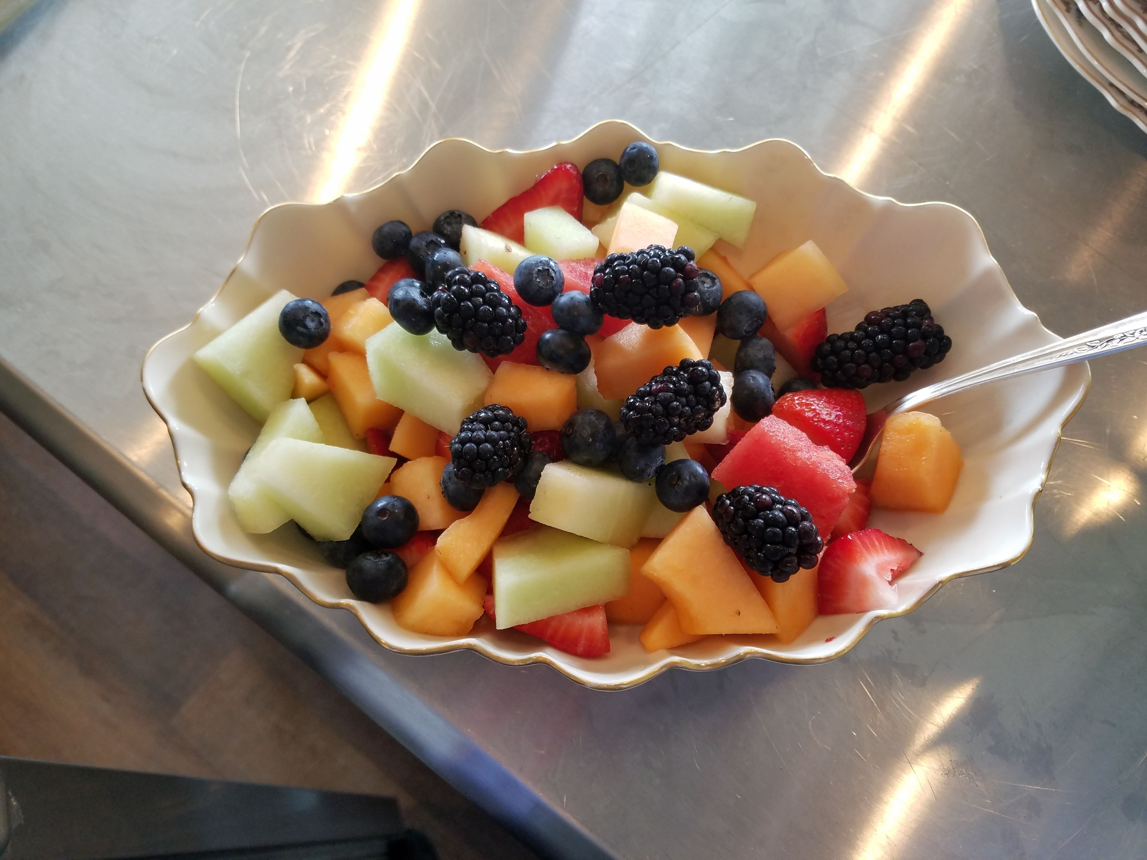 Uma tigela com frutas variadas, incluindo morangos, mirtilos, framboesas e melão cantaloupe.