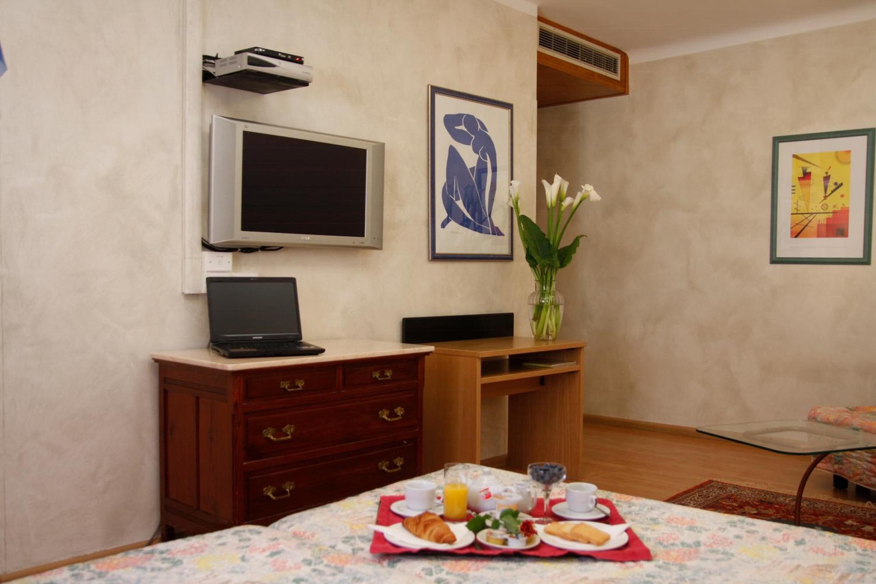 Quarto de hotel com cama, secretária com laptop, televisão e bandeja de café da manhã sobre a cama.