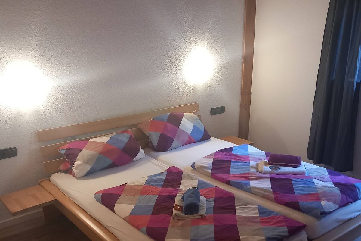 Uma cama de casal com estrutura de madeira, duas mesas de cabeceira e um encosto.