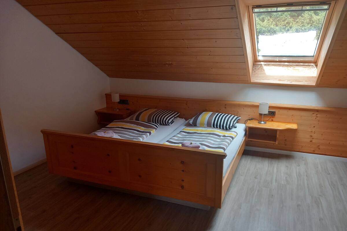 Quarto com cama de madeira, mesa de cabeceira e janela com vista para o verde.