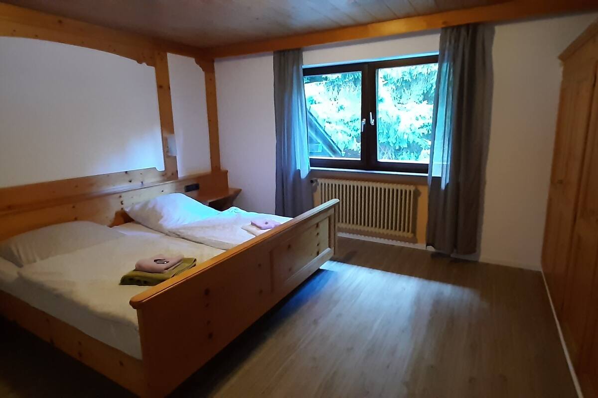 Uma cama de madeira num quarto com janela e radiador.