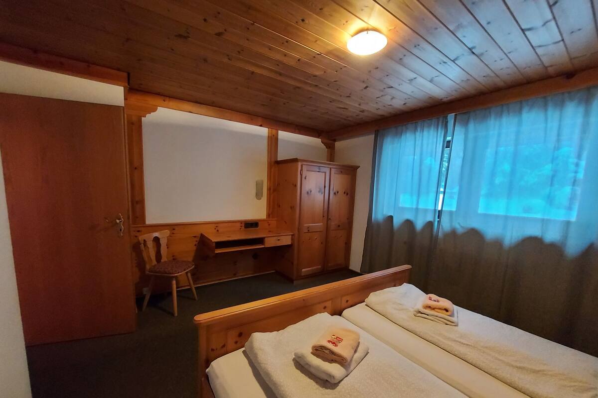 Quarto com painéis de madeira, uma cama, uma escrivaninha e uma cadeira.
