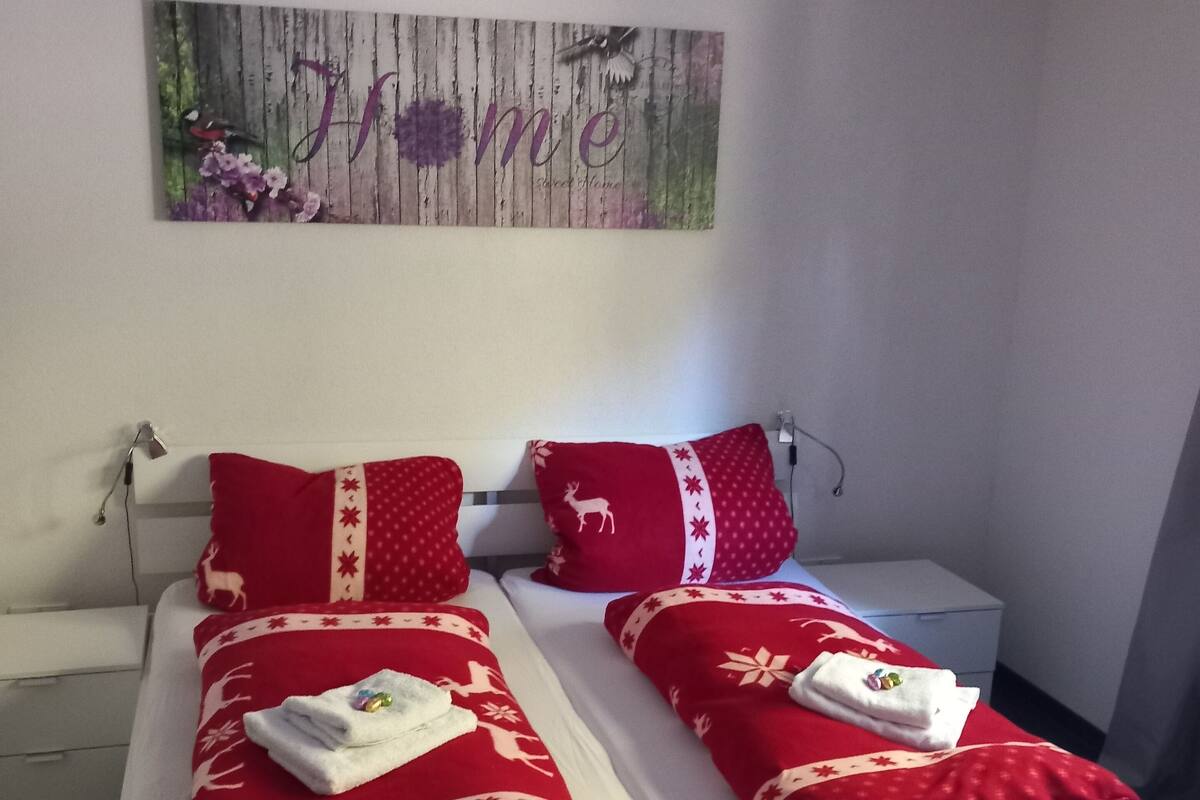 Uma cama de casal com roupa de cama vermelha e um letreiro com a palavra 'Home'.