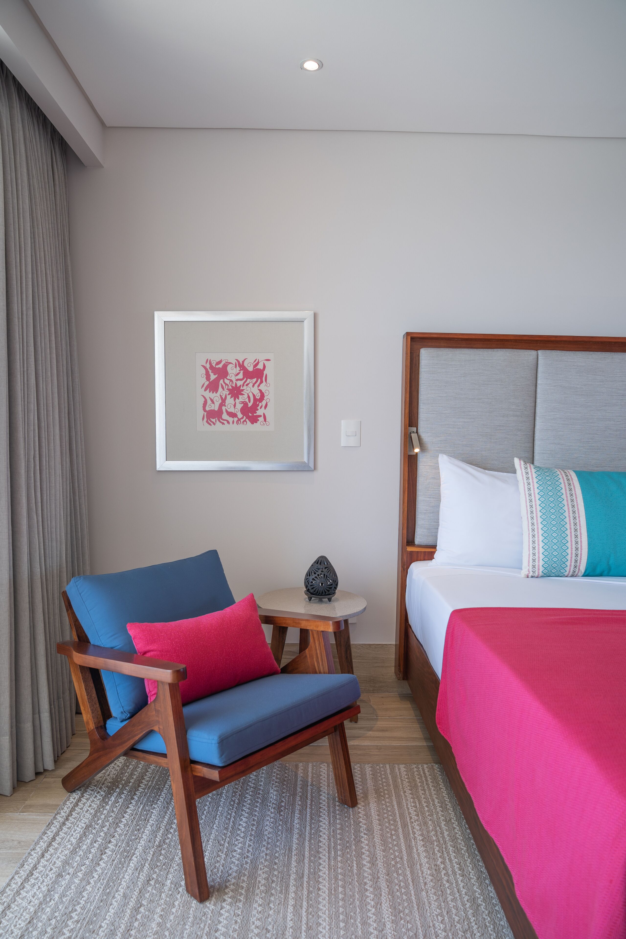 Quarto de hotel com cama, poltrona, mesa pequena e quadro na parede.