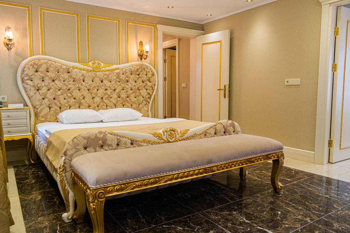 Um quarto luxuoso com uma cama grande, um banquinho combinando e uma mesinha de cabeceira.