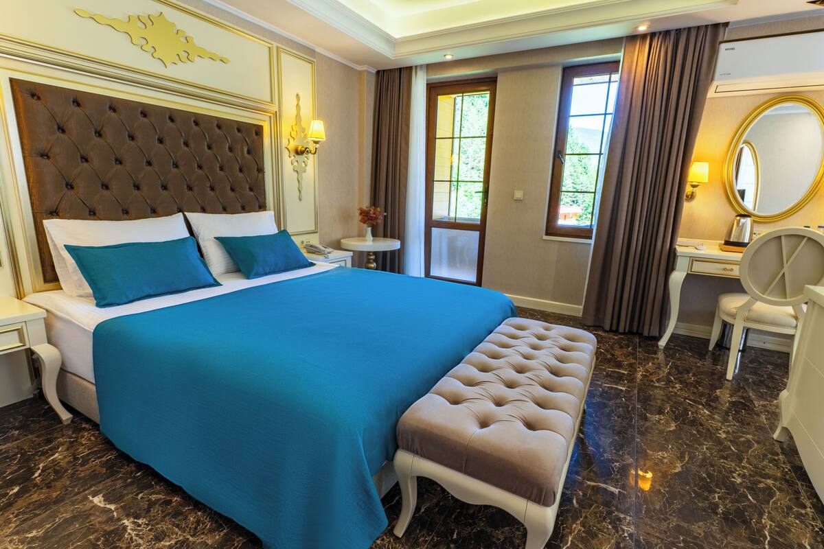 Quarto de hotel com uma cama grande, uma mesa de cabeceira, um espelho redondo e vista para o exterior.