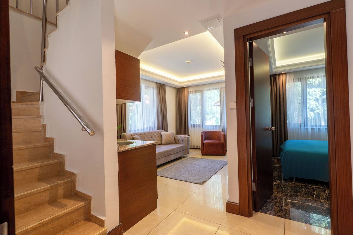 Quarto de hotel com escada de madeira, sofá, poltrona e cama com cobertura azul.
