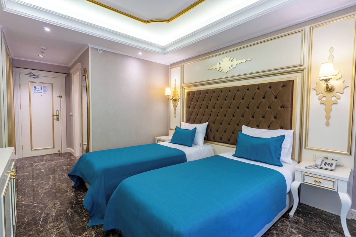 Quarto de hotel com duas camas, piso de mármore, cabeceira estofada, abajures laterais e mesa de cabeceira pequena com telefone.