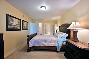 Quarto com cama, penteadeira, luminária e duas imagens emolduradas na parede.