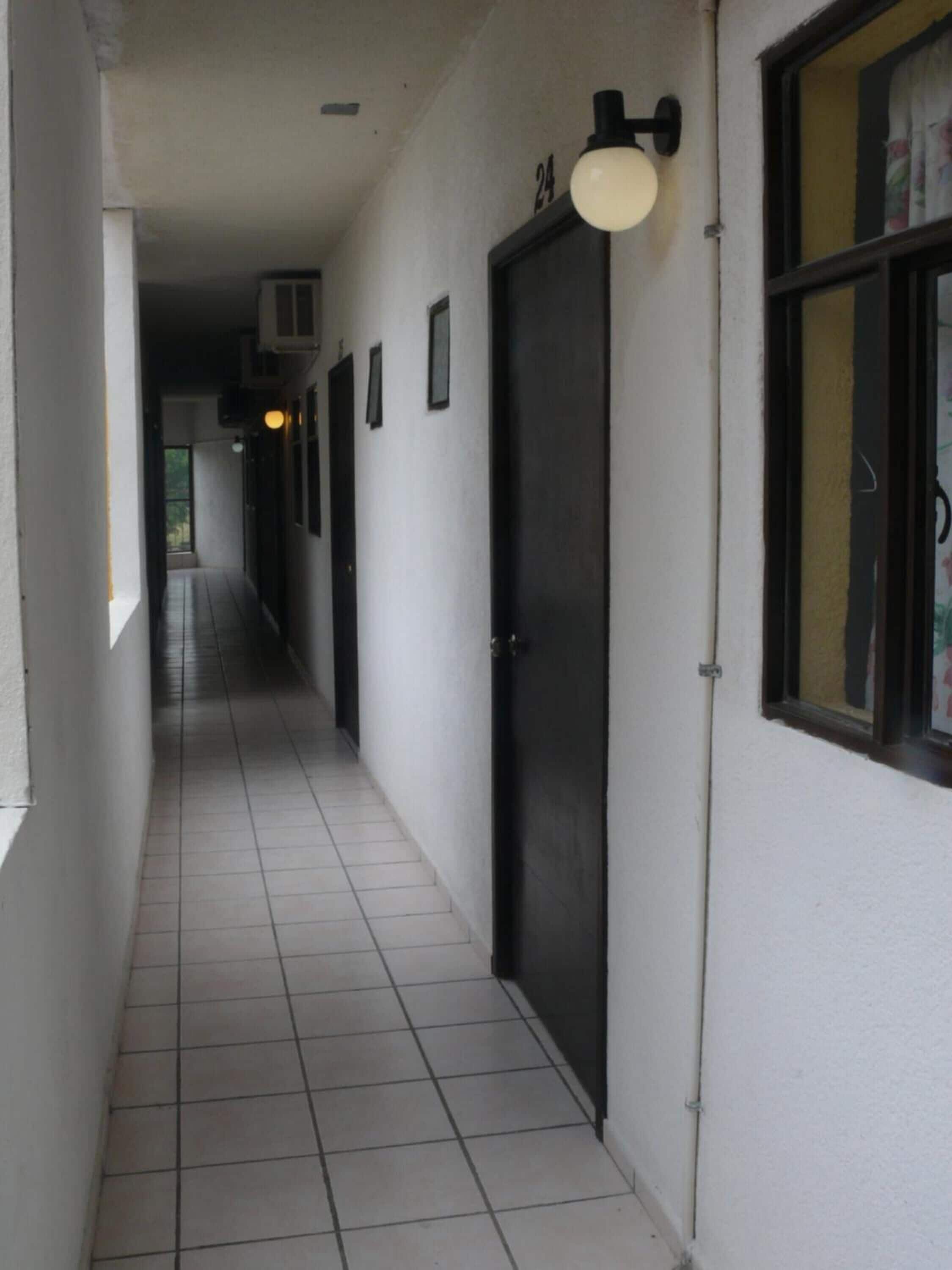 Um corredor com piso de azulejos, uma porta preta e um aplique na parede.