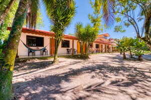 Um resort tropical com uma rede, palmeiras e um edifício com telhado vermelho.