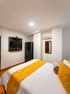 Quarto de hotel com cama, guarda-roupa, televisão fixada na parede e ar condicionado.