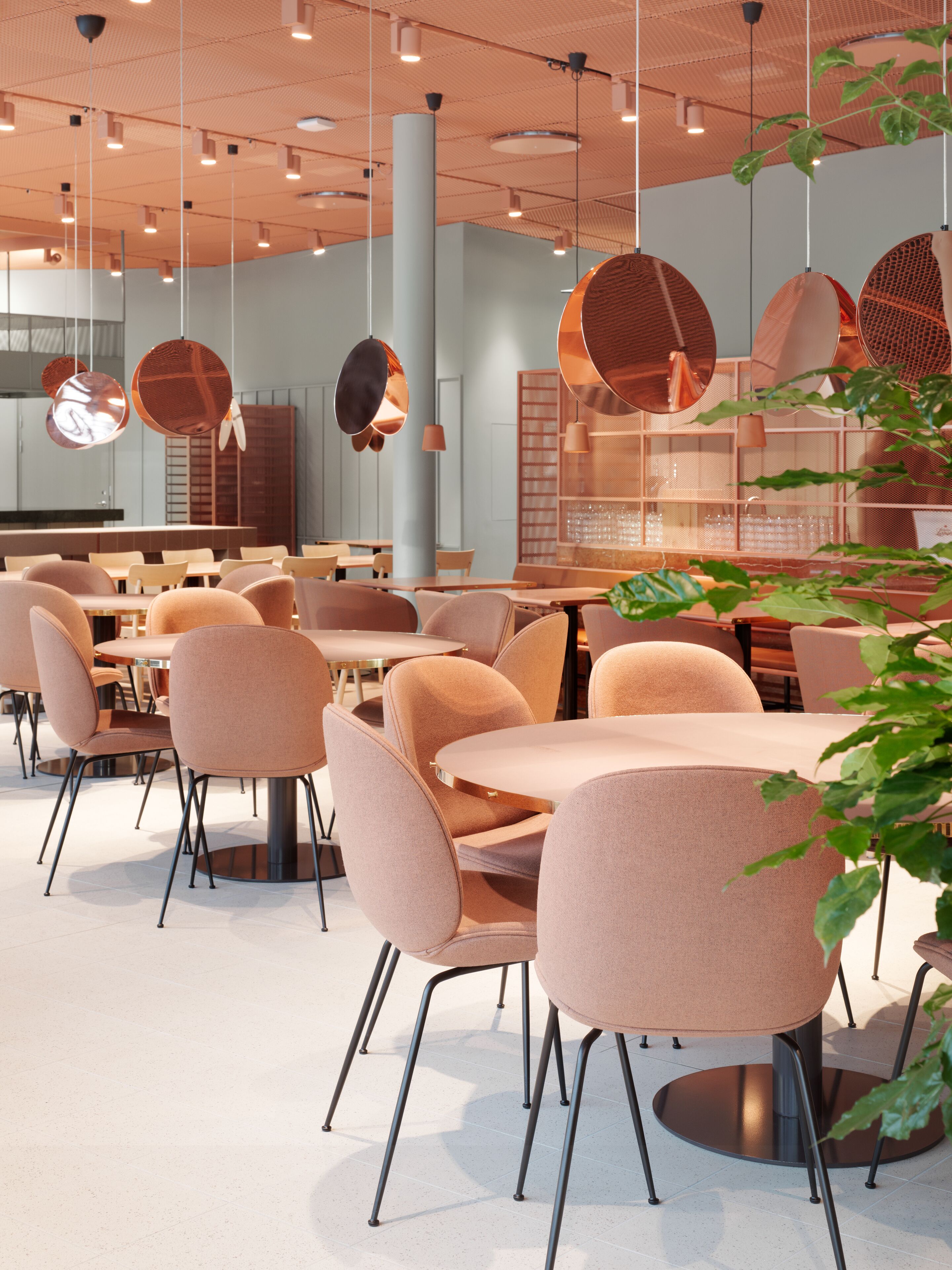 Um interior moderno com mesas e cadeiras redondas, iluminação pendente e uma planta em primeiro plano.