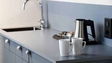 Uma cozinha moderna com uma cafeteira de aço inoxidável, duas chávenas brancas e um suporte de facas na bancada.