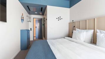 Quarto de hotel com uma cama grande, parede azul como detalhe, cabeceira de madeira e uma pequena mesa com cadeira.