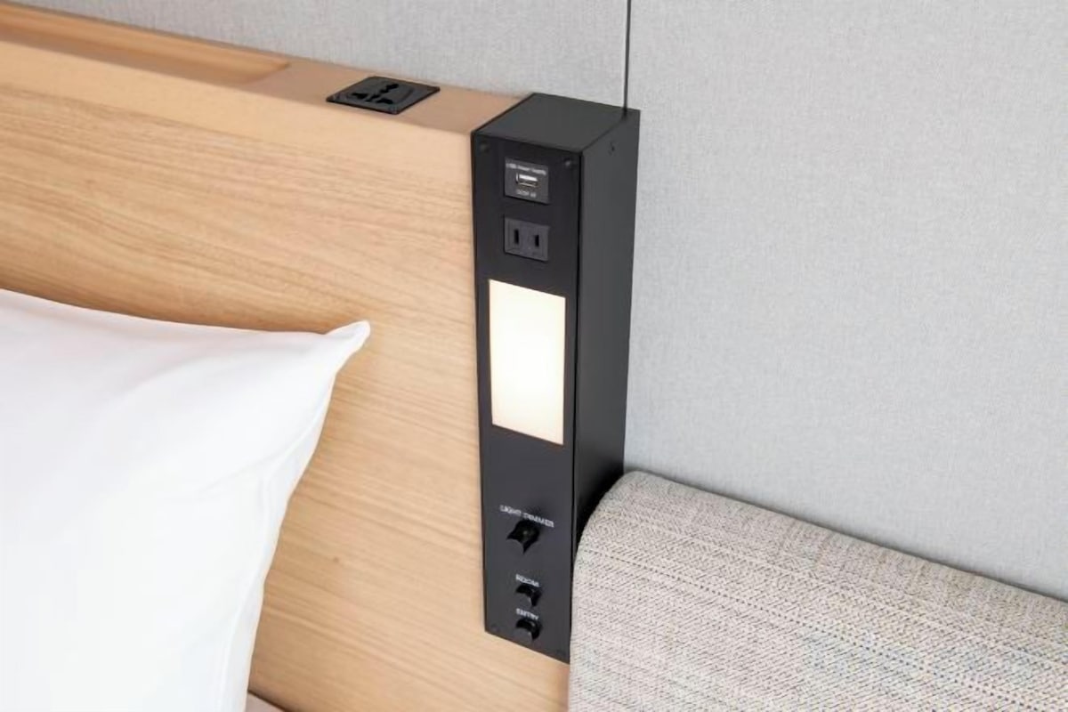 Cama com cabeceira, travesseiro e painel de controle com botões e interruptor.