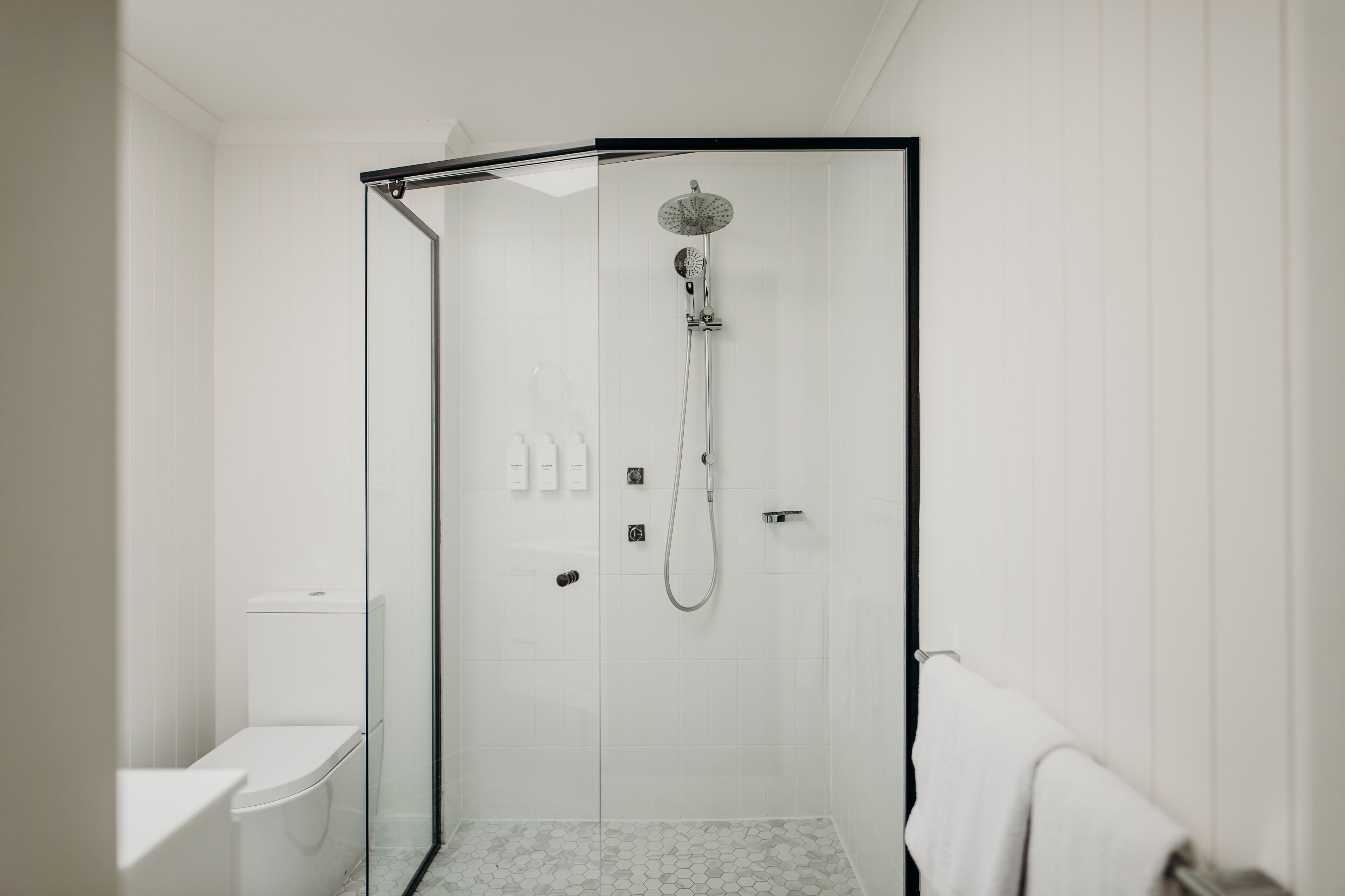 Uma casa de banho moderna com chuveiro de vidro, sanita e suporte para toalhas.