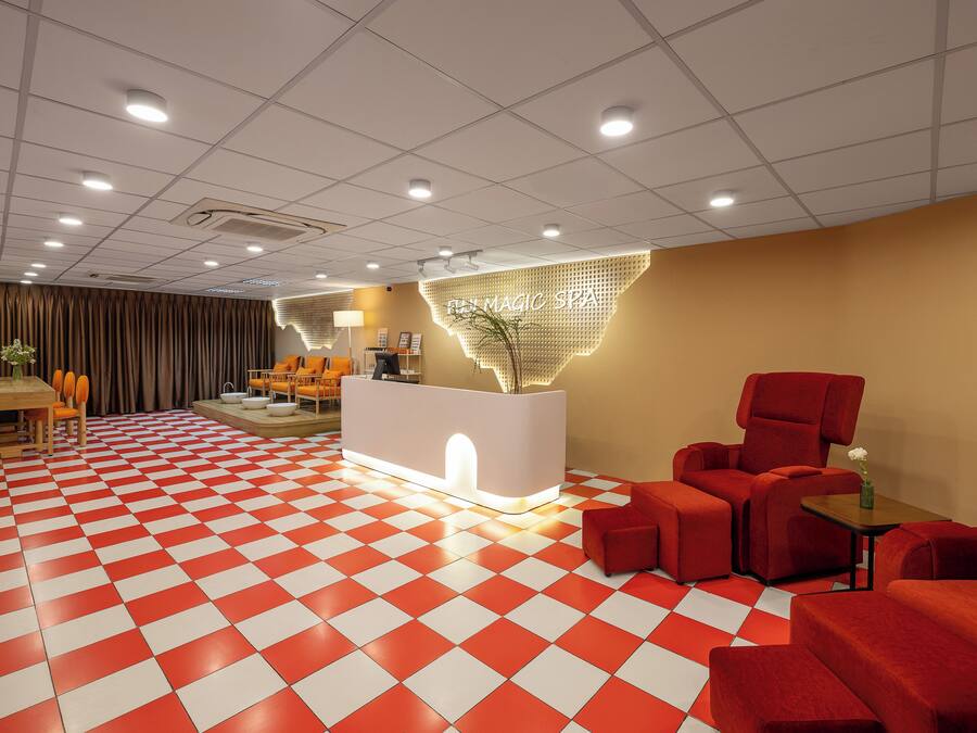 Uma área de recepção com piso xadrez, móveis vermelhos e brancos, e uma mesa de atendimento com luminária decorativa.