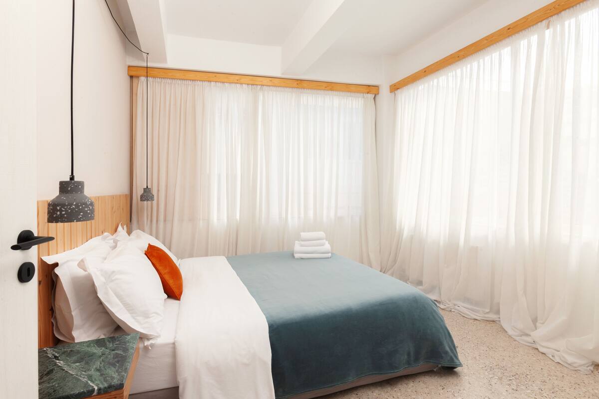 Uma cama bem arrumada com roupa de cama branca e verde-água, uma cabeceira de madeira e uma mesa de cabeceira de mármore.