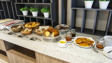Disposição de buffet com diversos alimentos, incluindo pão, doces e uma seleção de bebidas.
