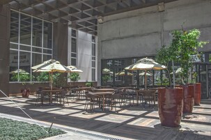 Espaço de estar ao ar livre com mesas, cadeiras, guarda-sóis e plantas em vasos.