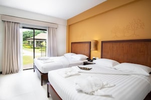 Quarto de hotel com duas camas, uma janela grande com cortinas, uma cabeceira de madeira e vista para um jardim.