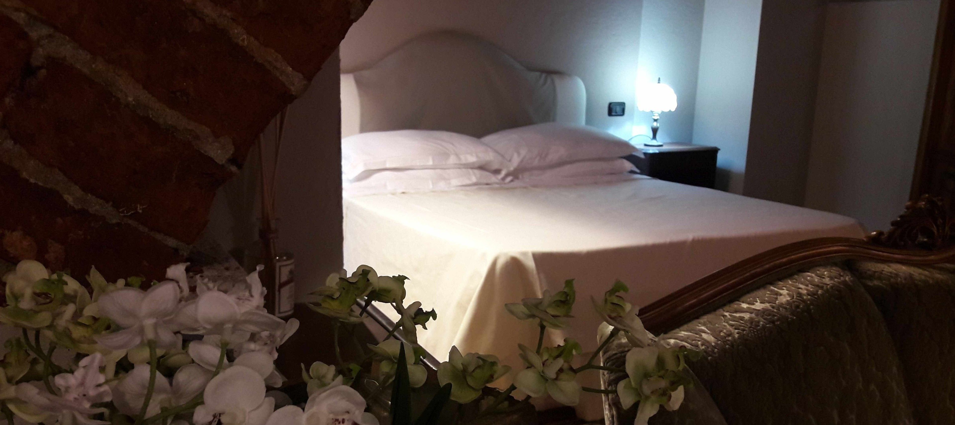 Cama bem arrumada com lençóis brancos, luminária de cabeceira e mesa de apoio.