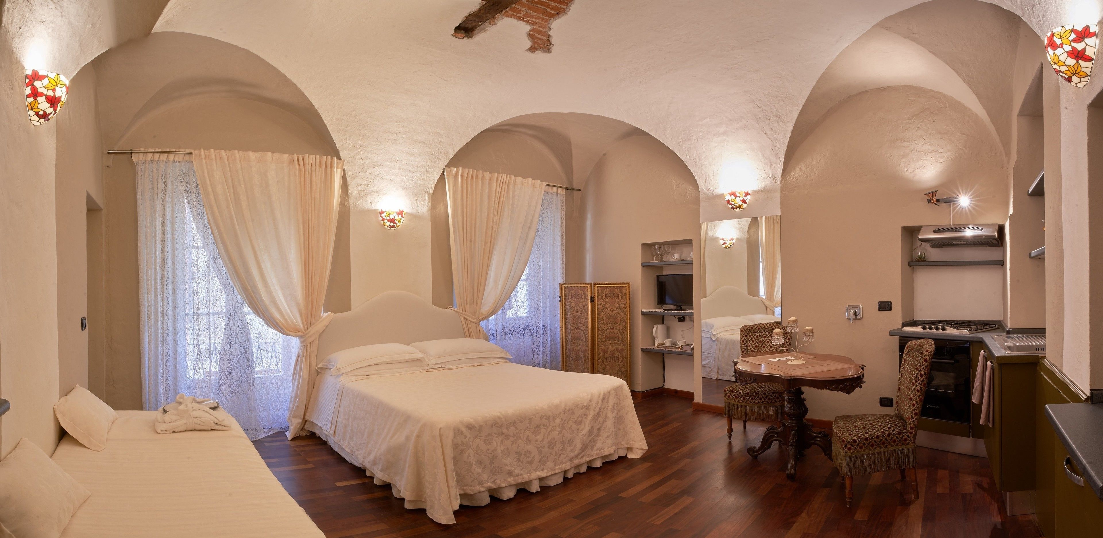 Quarto de hotel com duas camas, uma pequena mesa de jantar, uma cadeira, uma televisão e uma cozinha compacta.