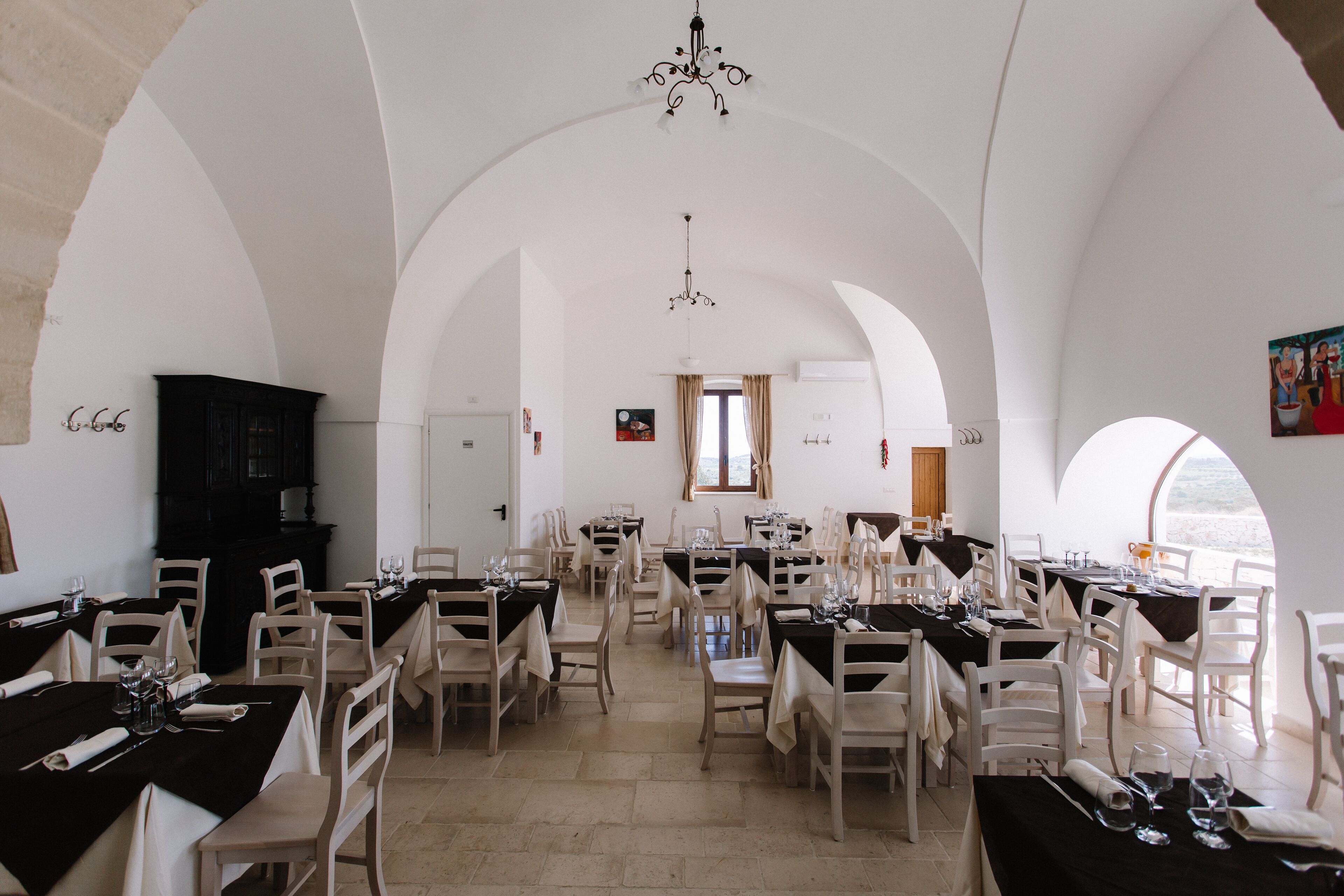 Uma sala de jantar com várias mesas e cadeiras, tetos abobadados e lustres.