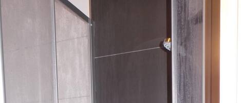 Divisória de chuveiro moderna com porta de vidro, chuveiro manual e dispensador de sabonete.