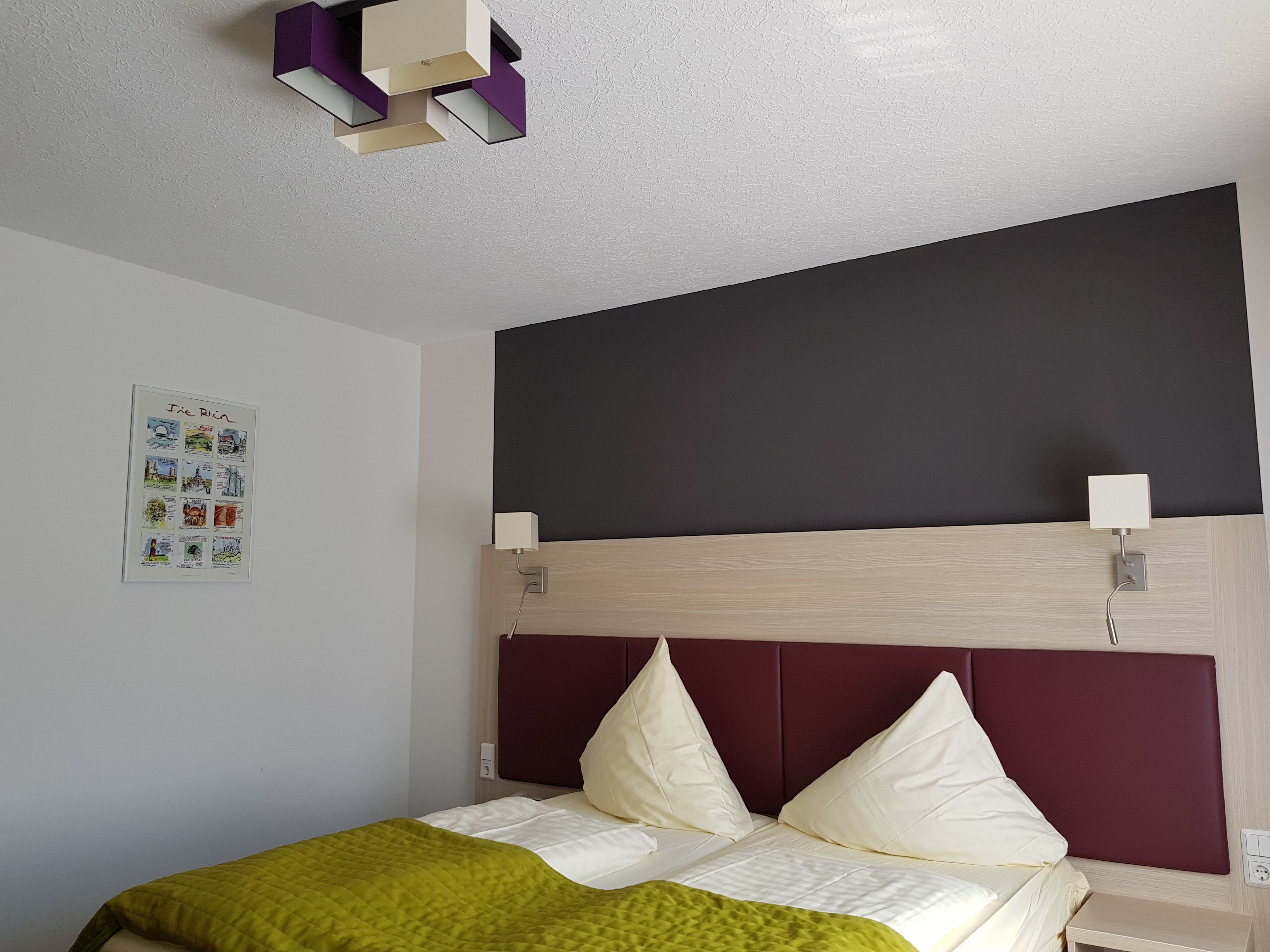 Quarto de hotel com cama, cabeceira, luminária na parede e um pôster.